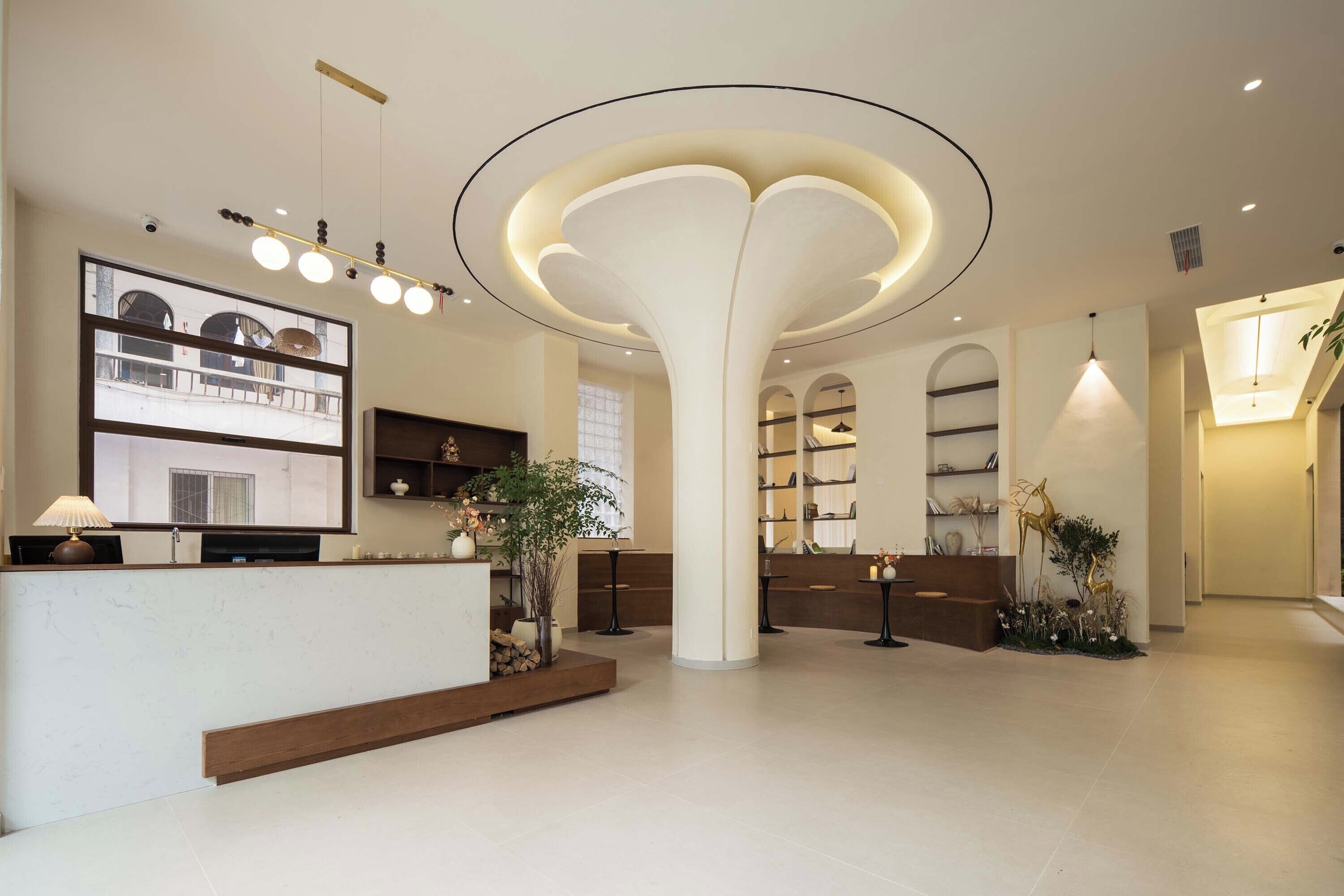 Um hall de hotel com uma coluna central, balcão de recepção e estantes de livros.