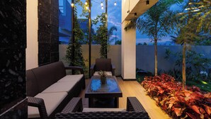 Uma área de varanda externa com móveis de vime, uma mesa de vidro e luzes de Natal.