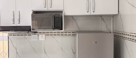 Uma cozinha com armários brancos, micro-ondas e geladeira.
