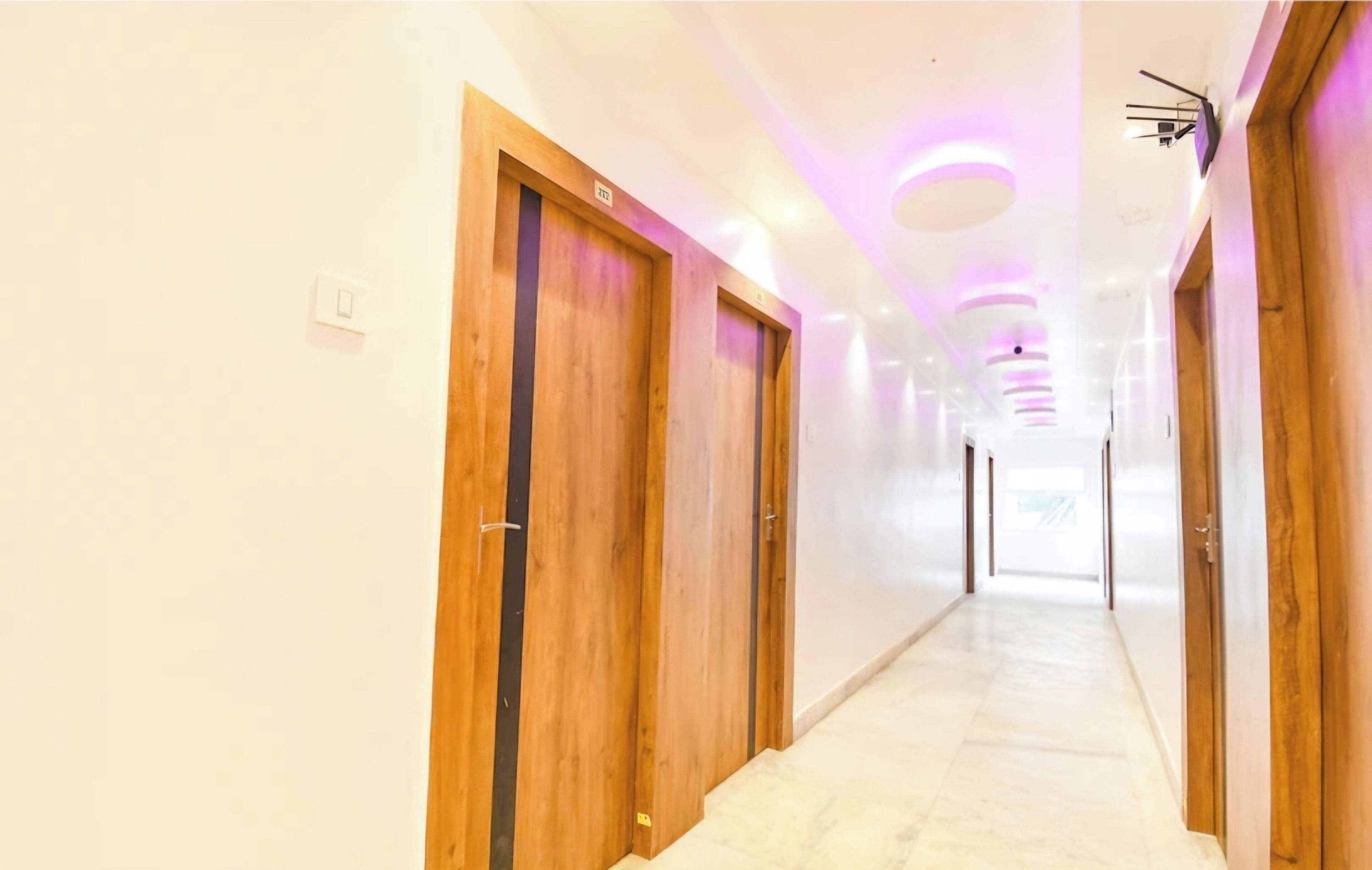 Um corredor com portas de madeira, piso de mármore e iluminação no teto.