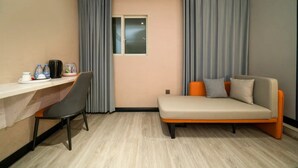 Um quarto pequeno com escrivaninha, cadeira, sofá e uma janela.