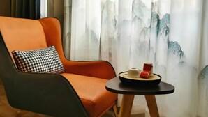 Quarto moderno com uma única cadeira laranja, uma almofada com padrão preto e branco, e uma pequena mesa redonda com duas xícaras e um suporte.