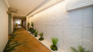Um corredor com parede texturizada, piso coberto por carpete e plantas em vasos.