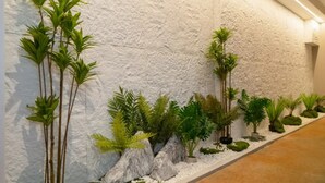 Um corredor com parede texturizada e uma fileira de plantas e pedras artificiais.