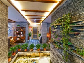 Um saguão de hotel com uma mesa de recepção de madeira, uma estante e um painel de plantas na parede.