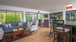 Uma sala de estar espaçosa com um sofá azul, poltronas estampadas, uma mesa de centro de madeira e um espaço de jantar com uma cadeira e mesa de madeira.