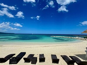 Uma praia com águas turquesa cristalinas, areal arenoso e espreguiçadeiras.