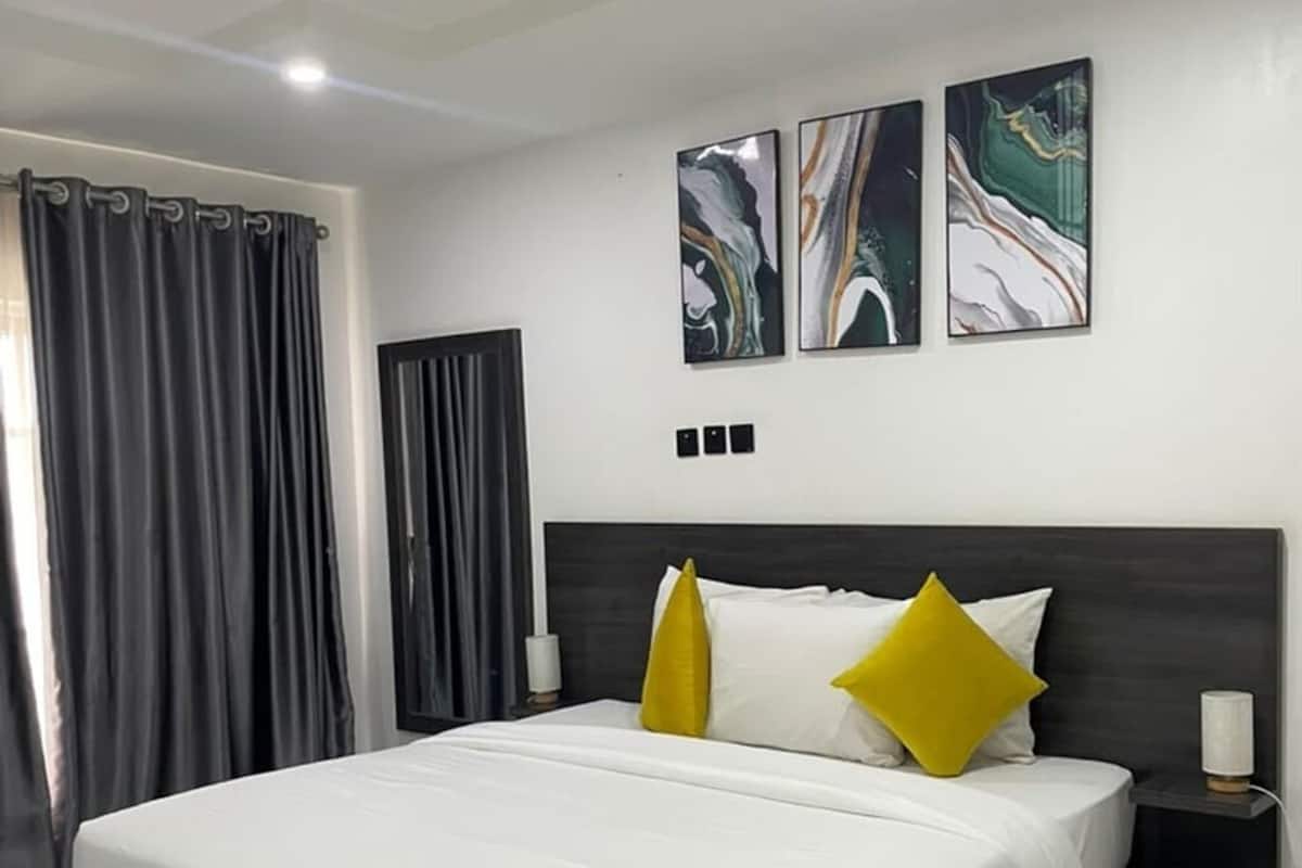 Quarto de hotel com cama, cortinas, arte na parede e mesa de cabeceira.