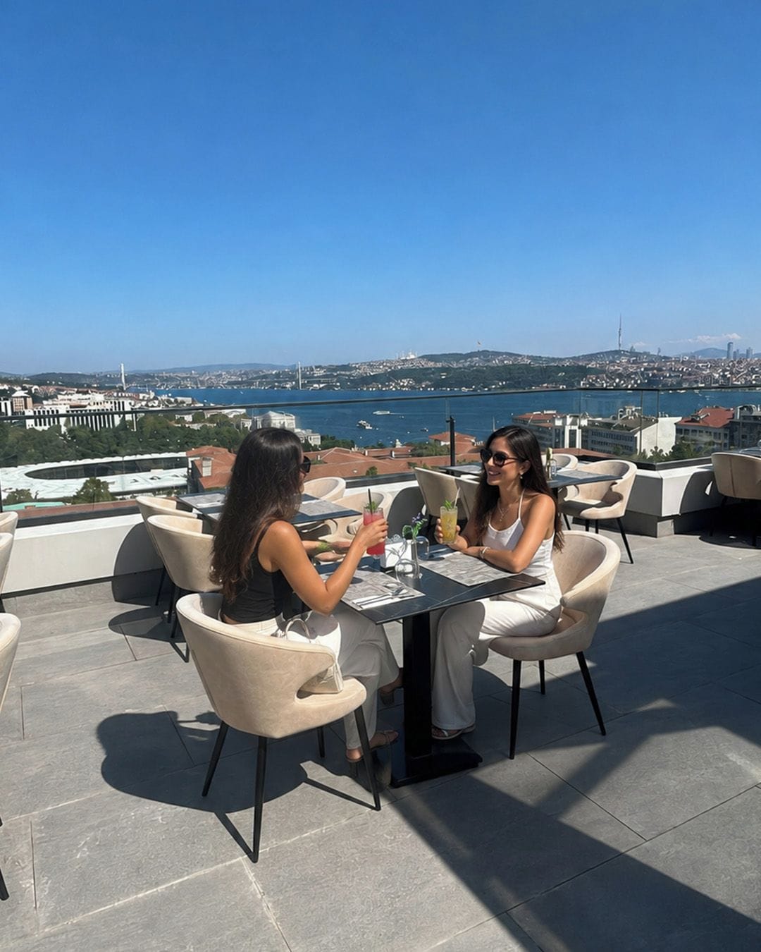 Duas pessoas sentadas em uma mesa ao ar livre, com vista para a cidade ao fundo.
