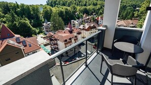 Varanda com mesa e cadeiras, com vista para uma cidade com edifícios de telhado vermelho e uma colina arborizada.