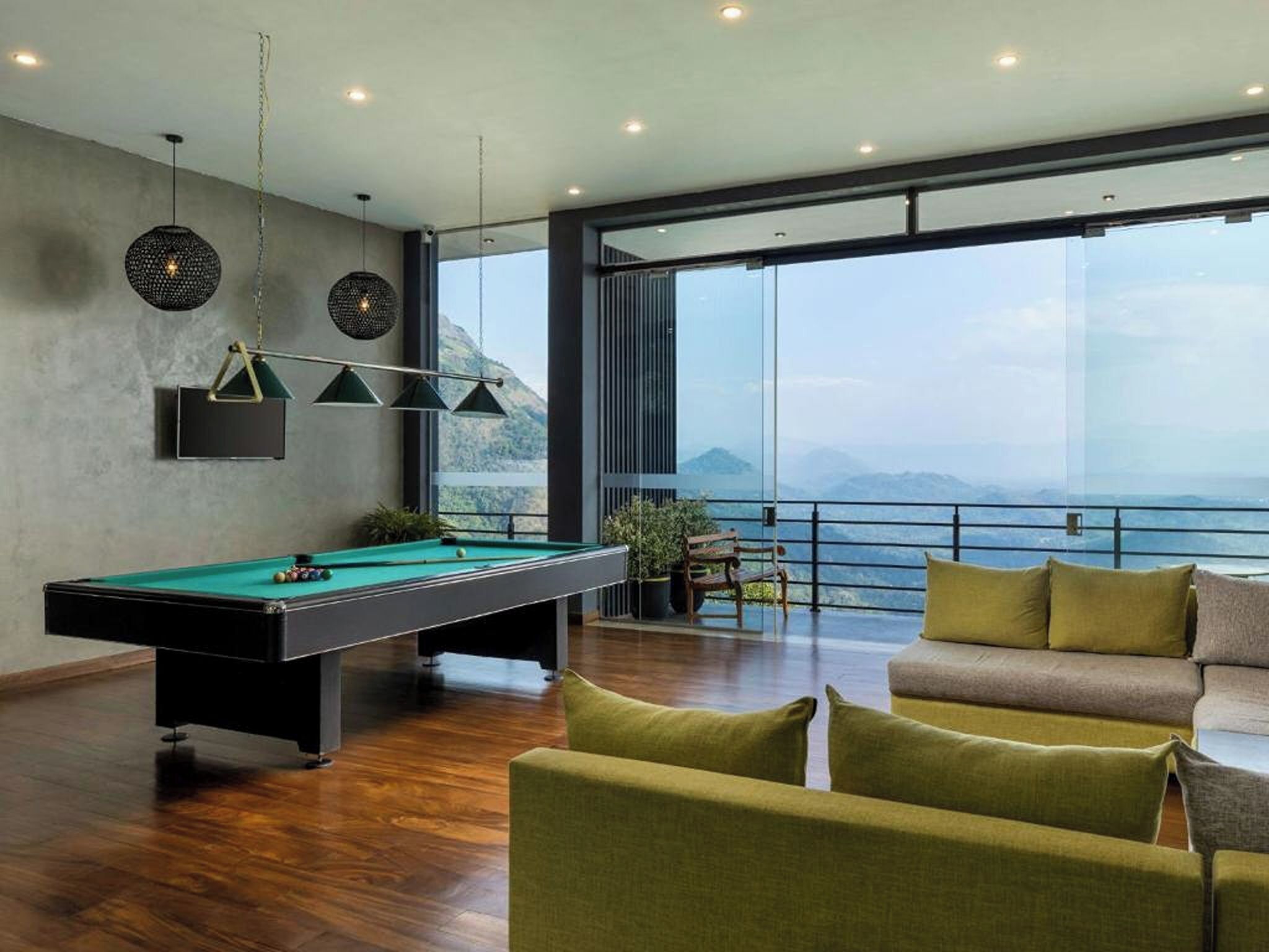 Quarto moderno com mesa de bilhar, almofadas verdes e vista para uma montanha.