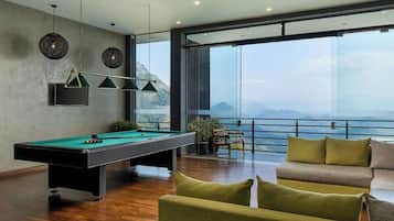Quarto moderno com mesa de bilhar, almofadas verdes e vista para uma montanha.