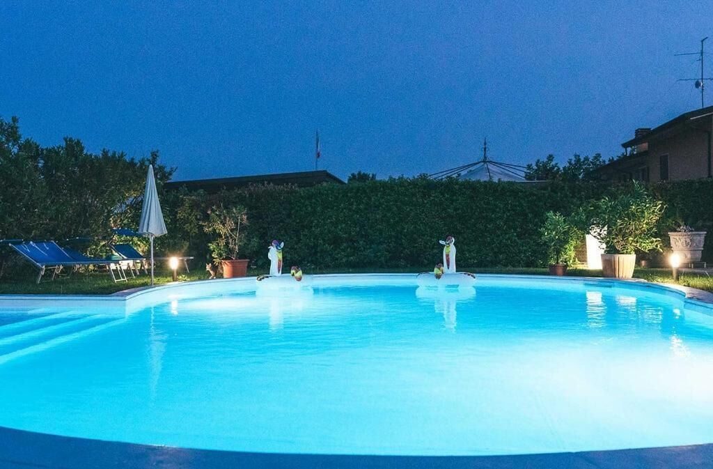Piscina com espreguiçadeiras e guarda-sóis, cercada por vegetação e edifícios.