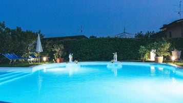 Piscina com espreguiçadeiras e guarda-sóis, cercada por vegetação e edifícios.