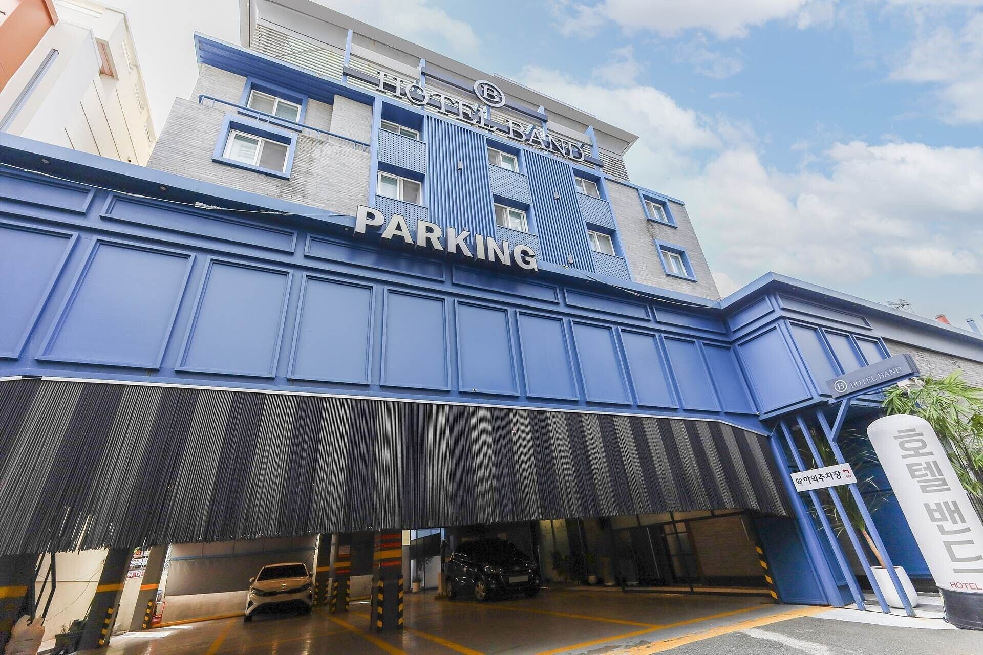 Entrada de hotel com fachada azul, sinalização de estacionamento e rampa de acesso visível.