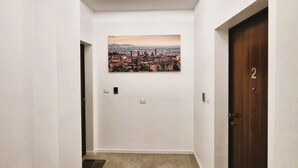 Um corredor com uma pintura de paisagem urbana, luminárias embutidas no teto, uma porta de madeira escura com um número e um tapete de entrada.