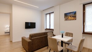 Uma sala de estar moderna com sofá, mesa de jantar e cadeiras, uma TV de tela plana na parede e um quadro na parede.