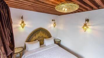 Uma cama com cabeceira decorativa, duas luminárias na parede e um lustre.