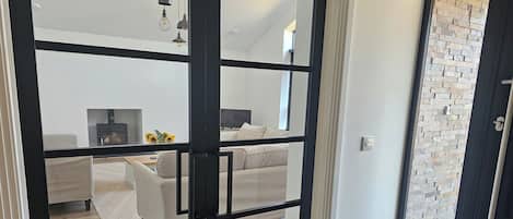 Um interior moderno com uma porta de vidro que dá para uma sala de estar com sofá, mesa de centro e lareira.