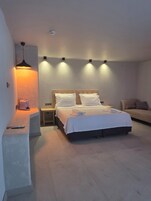 Quarto moderno com cama, mesas de cabeceira, um banco e um sofá.