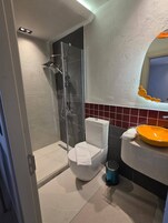 Uma casa de banho com cabine de duche em vidro, sanita branca, lavatório com cuba amarela e espelho com moldura decorativa.