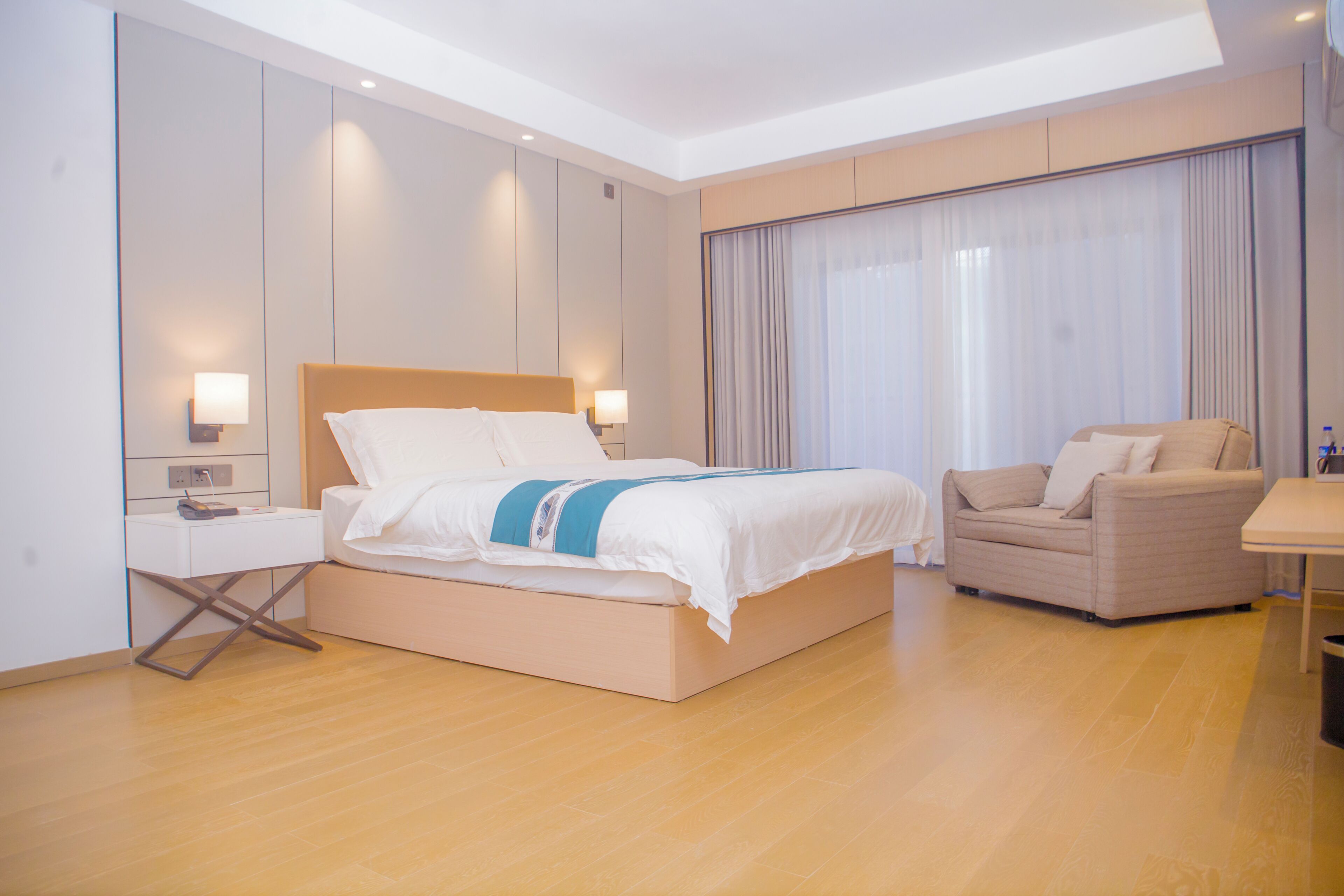 Quarto de hotel moderno com uma cama grande, um sofá, uma escrivaninha e uma janela com cortinas.