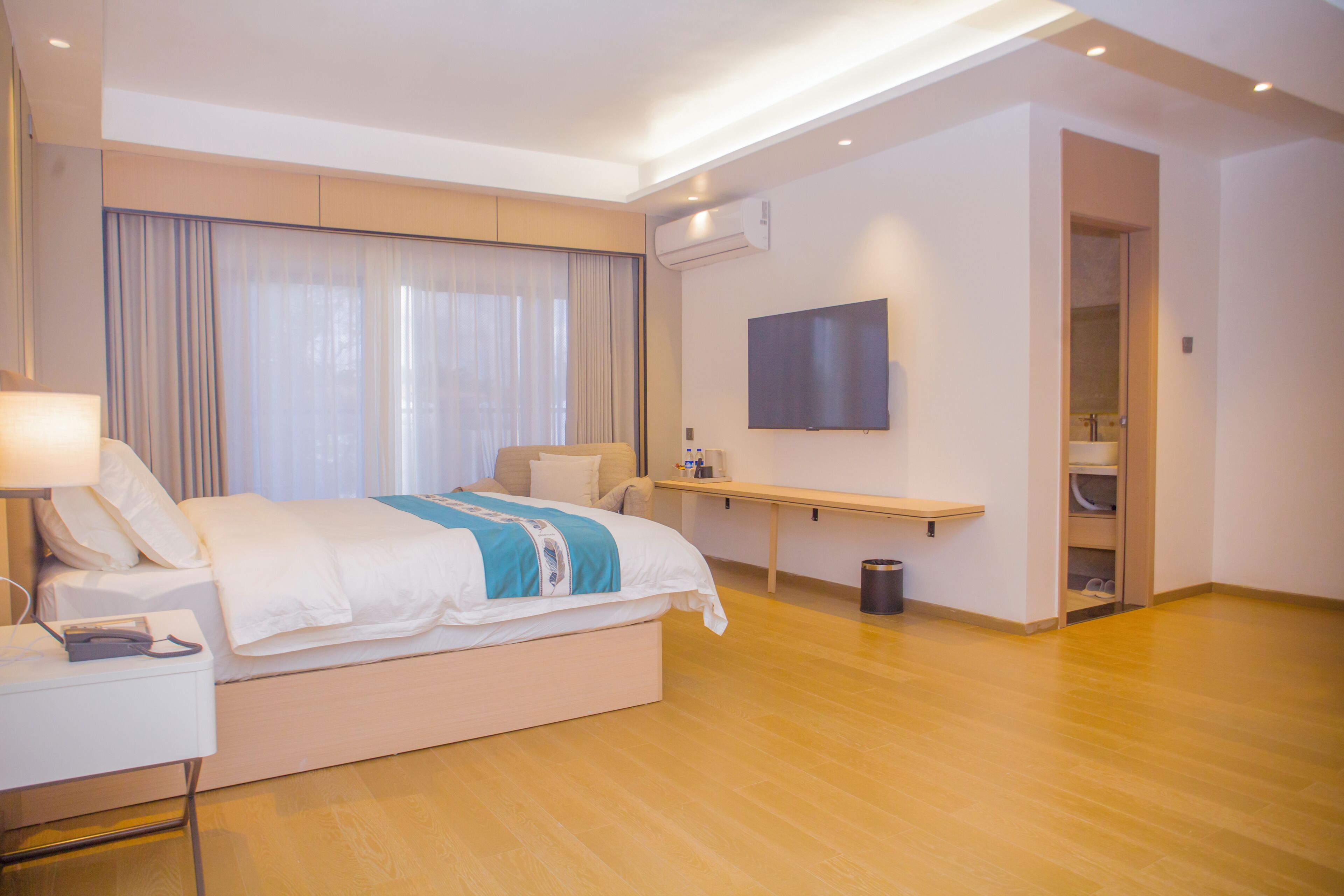 Quarto de hotel moderno com uma cama grande, mesa de cabeceira e televisão na parede.