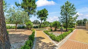 Um caminho pavimentado, árvores e um canteiro de jardim circular em uma área ajardinada.
