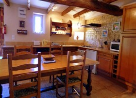 Uma mesa de jantar de madeira com cadeiras, uma cozinha com paredes de pedra, armários de madeira e um micro-ondas.