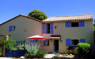 Uma casa de dois andares com telhado de telhas, porta da frente e um pequeno alpendre com um guarda-sol vermelho.