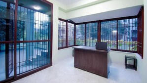 Quarto com uma escrivaninha, janelas amplas com grades de metal e vista para o verde lá fora.