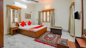 Quarto com cama, mesas de cabeceira, escrivaninha, cadeira, ventoinha de teto e televisão.