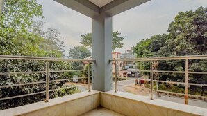 Uma varanda com guarda-corrimão de metal, piso de concreto e vista para vegetação e edifícios ao longe.
