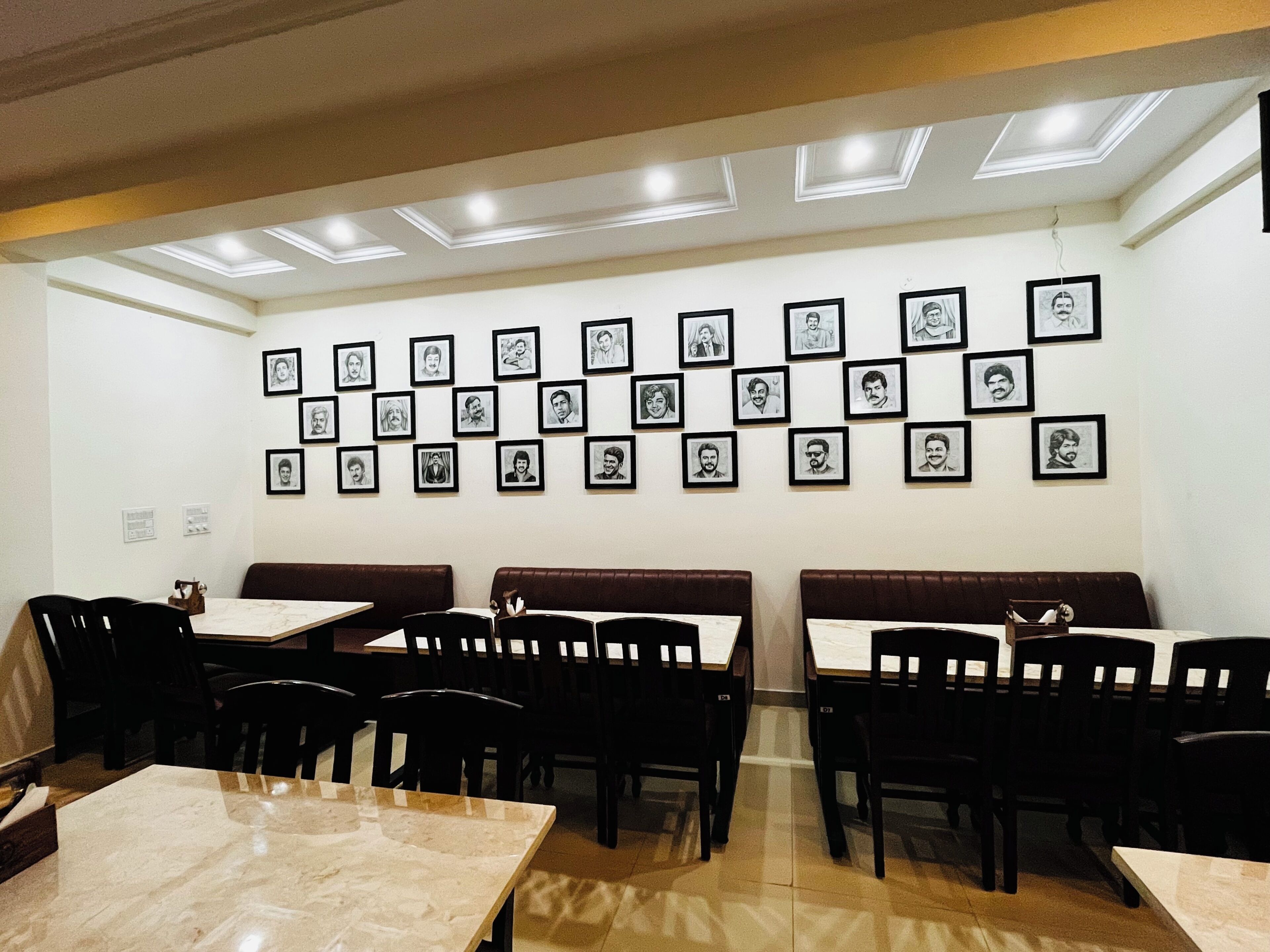 Um restaurante com cabines e mesas, teto com iluminação embutida e parede decorada com retratos preto e branco emoldurados.