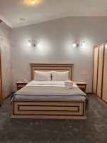 Quarto com uma cama grande, mesas de cabeceira, guarda-roupa e luminárias fixadas na parede.