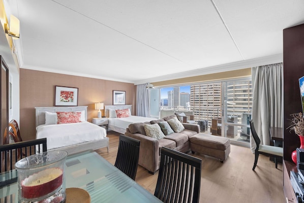 Quarto de hotel com cama, dois sofás, mesa de jantar, cadeiras e uma janela grande com vista para a cidade.