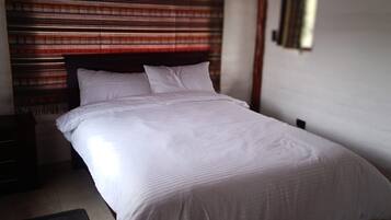 Uma cama bem arrumada em quarto de hotel, com cabeceira listrada, mesa de cabeceira e luminária fixada na parede.