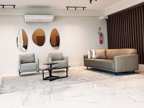 Um lobby moderno com um sofá, duas poltronas, uma mesa de centro e três espelhos fixados na parede.
