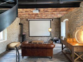 Quarto com sofá de couro, tela de projetor e escrivaninha de madeira com luminária.
