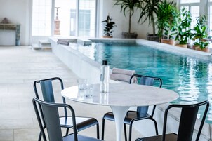 Uma área de piscina interna com uma mesa redonda e cadeiras, uma garrafa e copos.