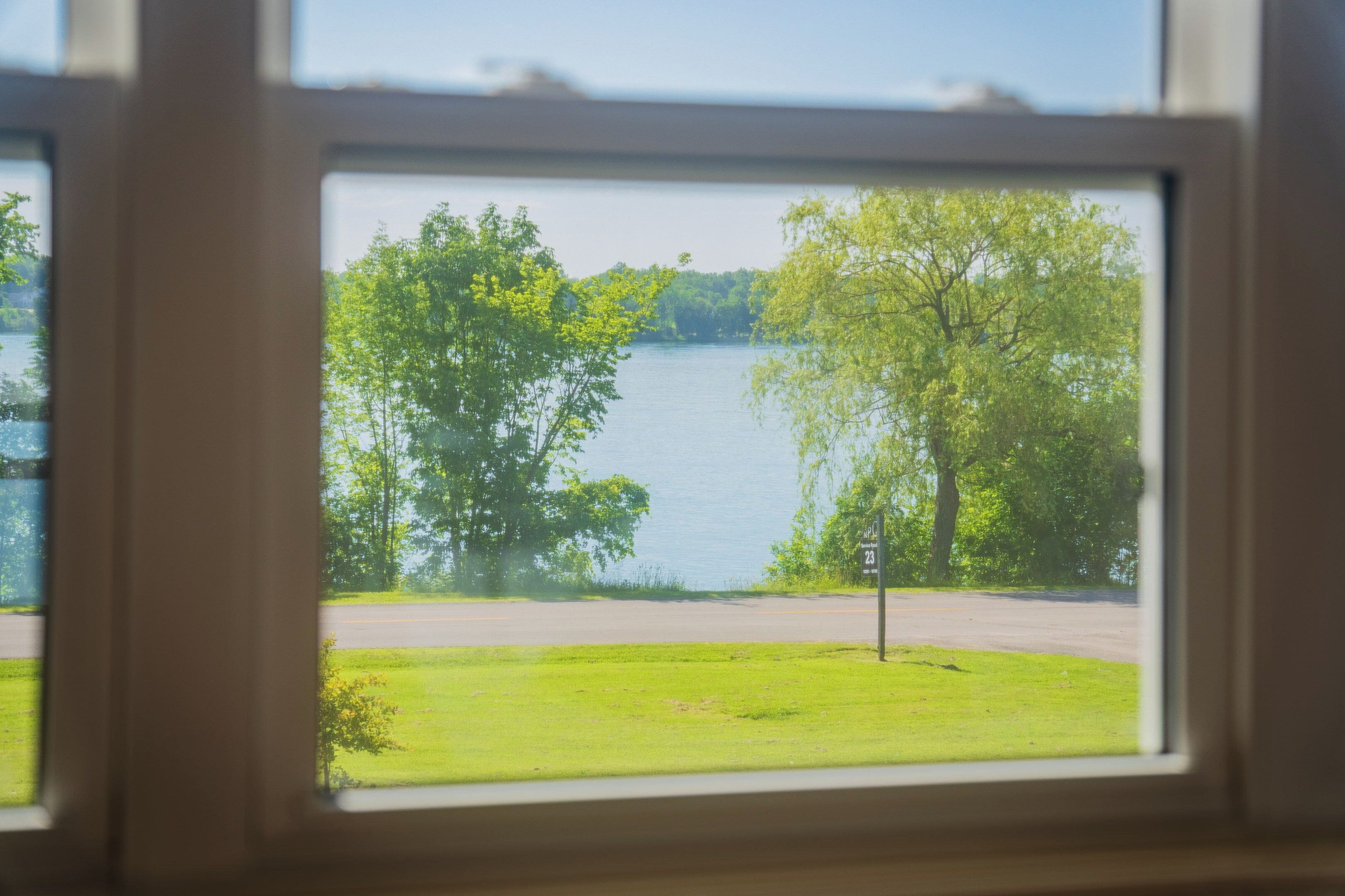 Vista pela janela de um lago com árvores e um estacionamento.