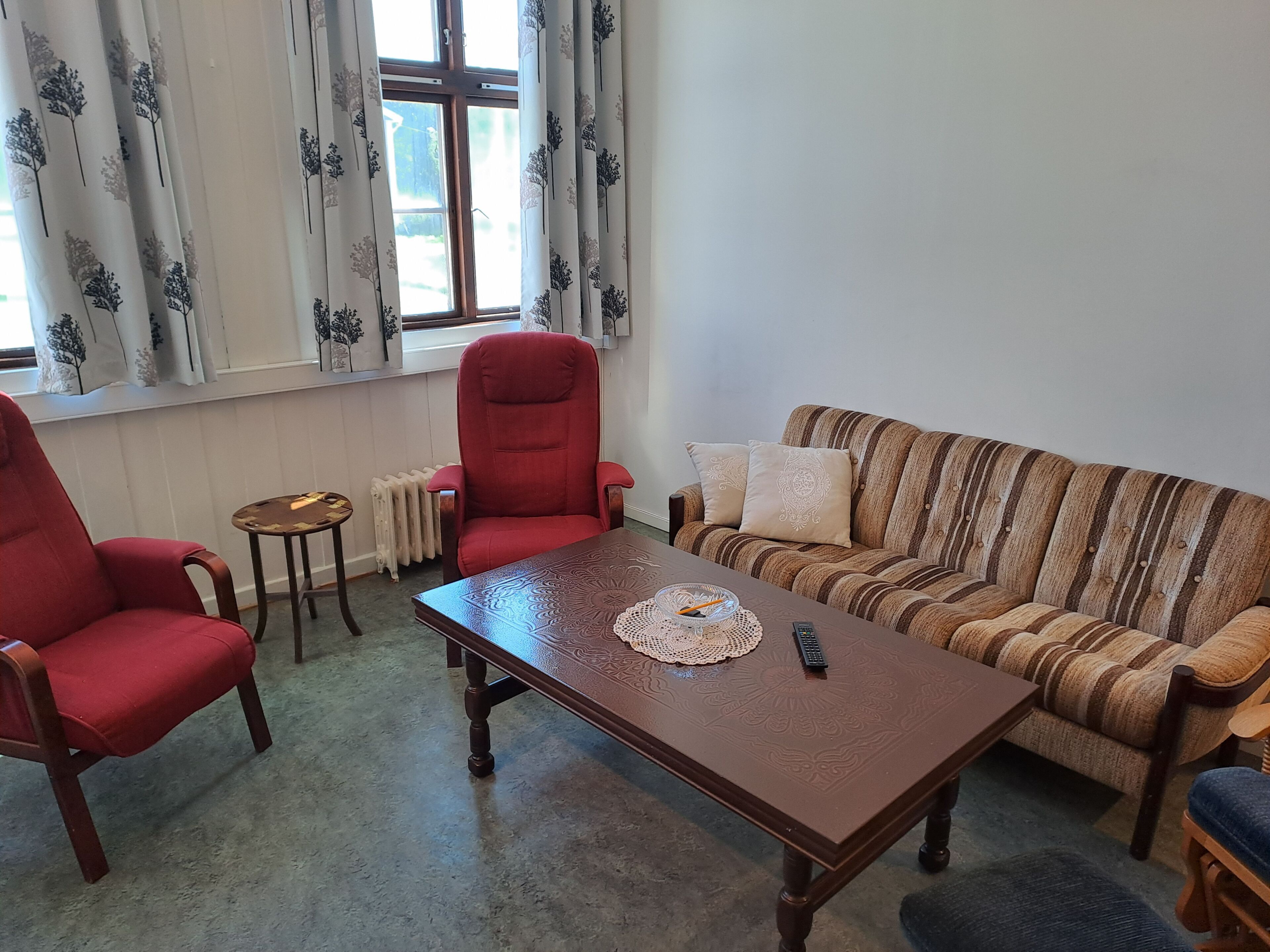 Uma sala de estar com uma poltrona vermelha, um sofá listrado, uma mesa de centro de madeira e uma mesinha lateral.