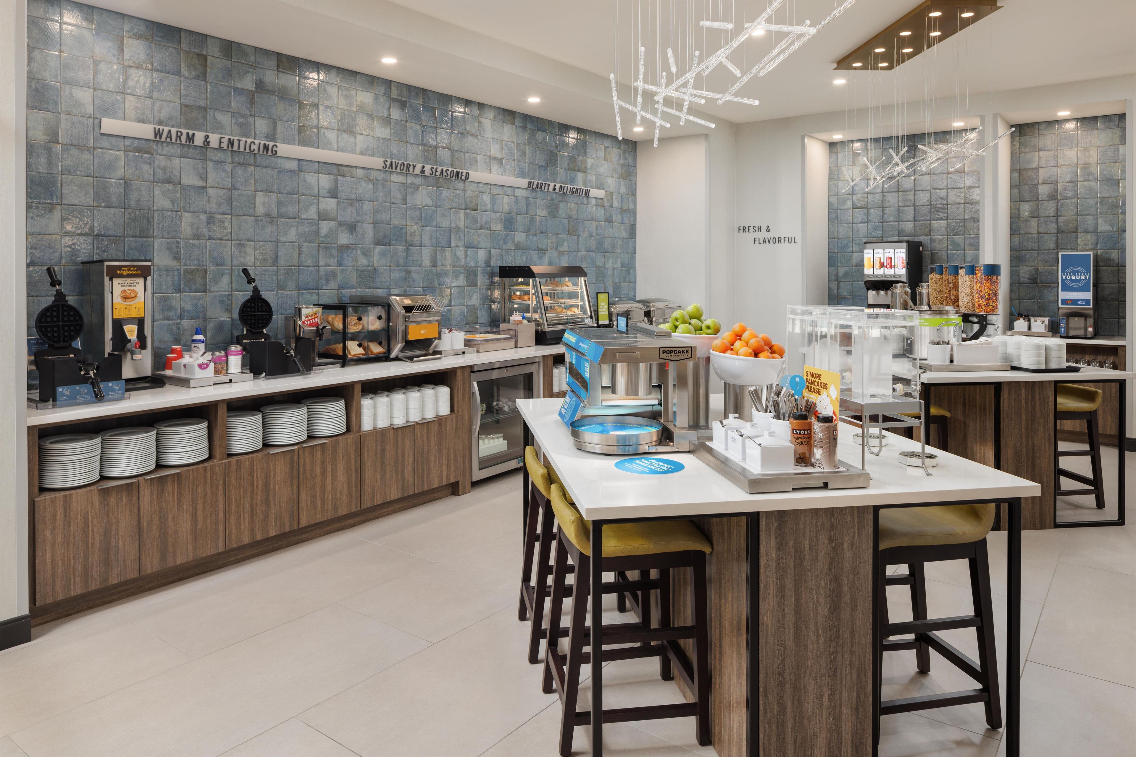 Uma moderna área de refeições com máquinas de waffle, cafeteira e dispensador de iogurte.