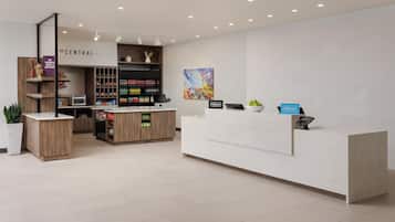 Uma área de recepção de hotel com design moderno, incluindo um balcão de atendimento, um quiosque de autoatendimento e um balcão de entrega de comida.
