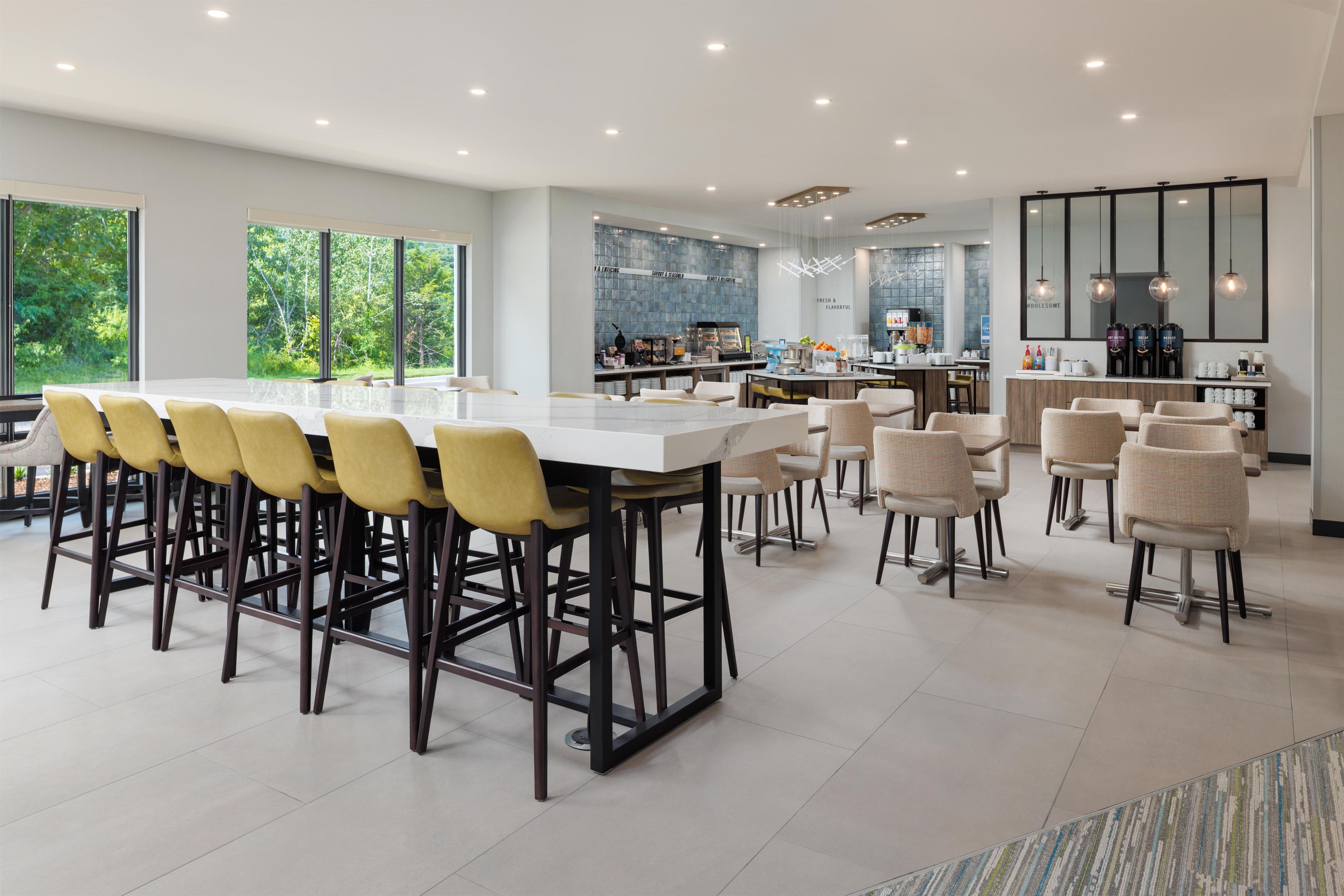 Cozinha moderna com espaço de bar, grandes janelas e vista para o verde.