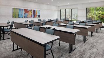 Uma sala de conferências com várias mesas e cadeiras, janelas amplas e arte abstrata na parede.