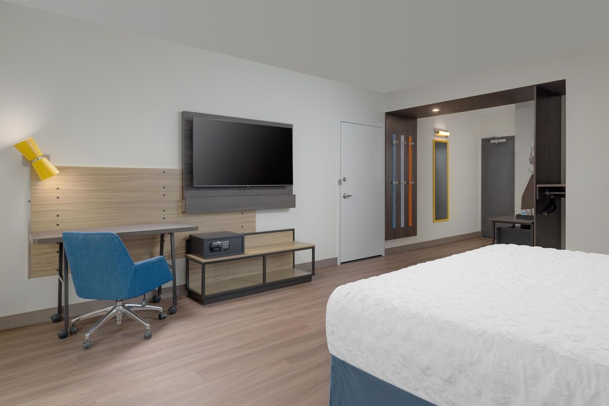 Quarto de hotel com uma cama, uma escrivaninha com cadeira, televisão e guarda-roupa.