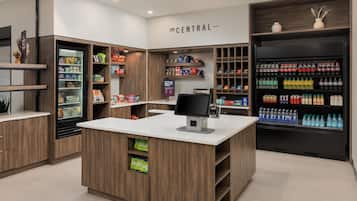 Um espaço comercial moderno com um balcão central, prateleiras repletas de lanches, bebidas e um expositor refrigerado.