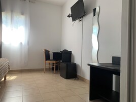 Quarto com cama, escrivaninha, cadeira, televisão e espelho.