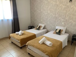 Quarto de hotel com duas camas, cada uma com colcha marrom e roupa de cama branca, parede texturizada e uma pequena mesa de cabeceira com luminária.